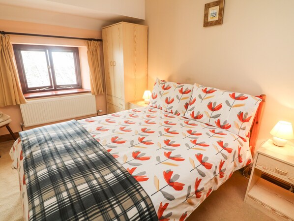 Quarto com cama, mesa de cabeceira, guarda-roupa, janela com cortinas e radiador.