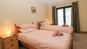 Quarto com duas camas de solteiro, mesa de cabeceira com abajur, cômoda e janela com cortinas.
