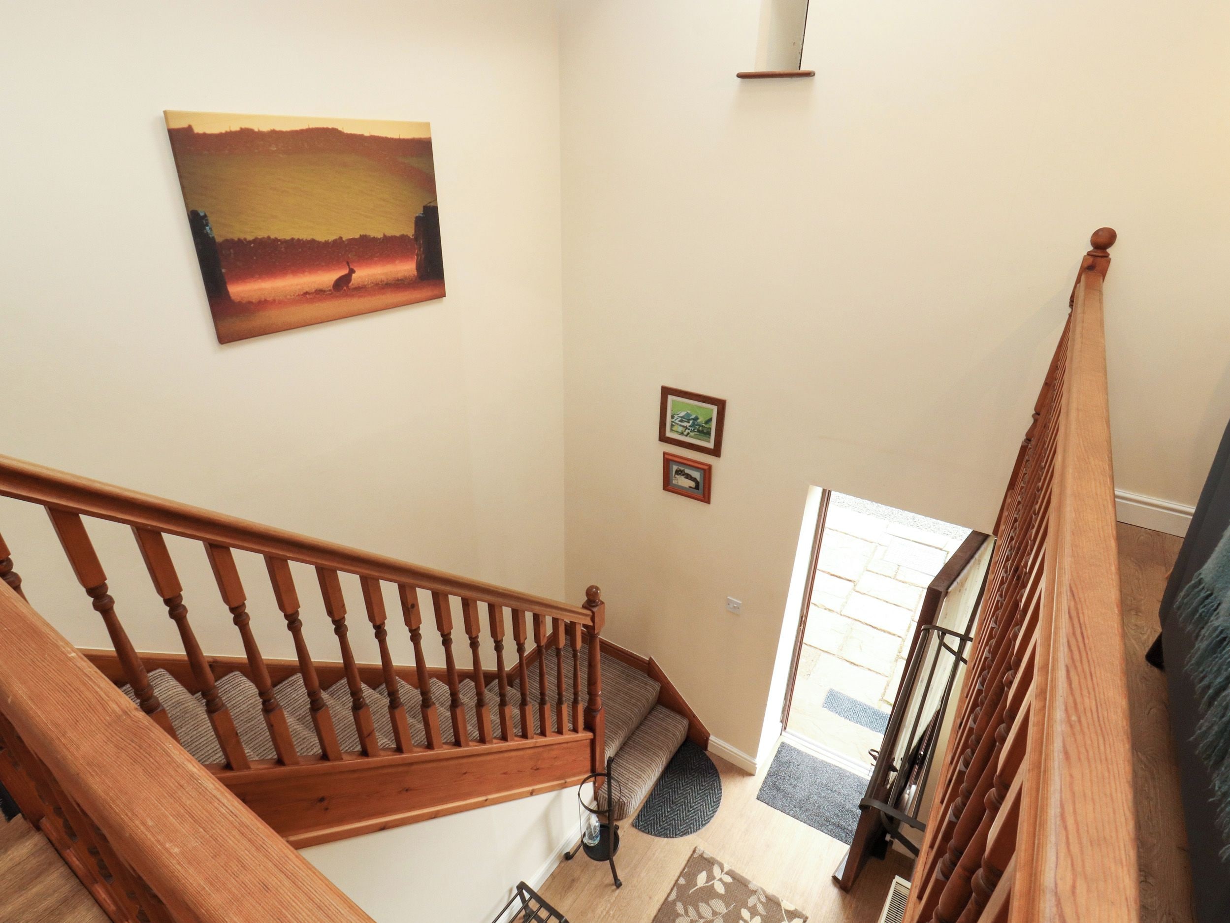 Escada de madeira com corrimão, porta que dá para área externa e um quadro na parede.