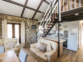 Uma sala de estar aconchegante com parede de pedra, escada de madeira e área de cozinha.
