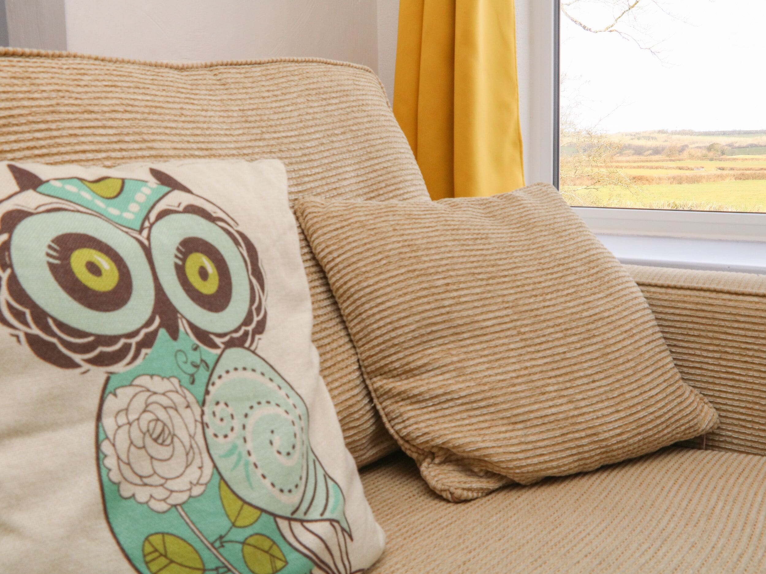 Um sofá com uma almofada estampada e uma janela com vista para um campo.