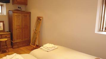 Quarto com duas camas de solteiro, guarda-roupa de madeira, escrivaninha com cadeira e janela com cortinas.