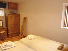 Quarto com duas camas de solteiro, guarda-roupa de madeira, escrivaninha com cadeira e janela com cortinas.