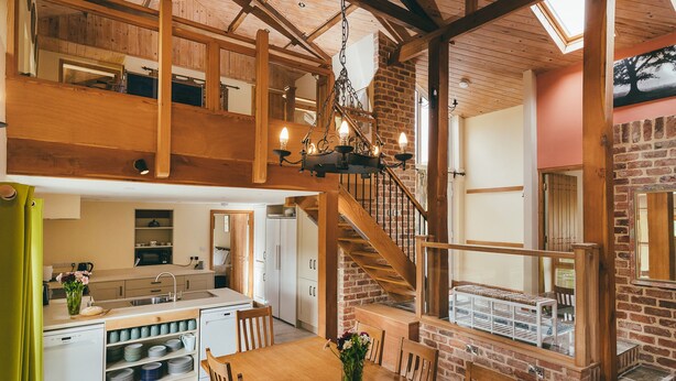 Uma ampla sala de estar no estilo loft, com escada de madeira, mesa de jantar e cozinha.