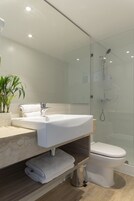 Uma casa de banho moderna com chuveiro separado por vidro, lavatório branco e sanita.