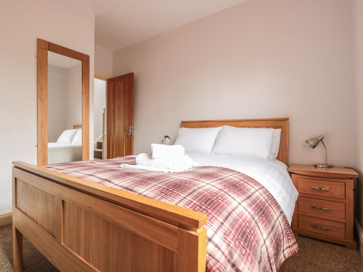 Um quarto com cama de madeira, mesa de cabeceira com abajur, guarda-roupa de madeira e espelho na parede.