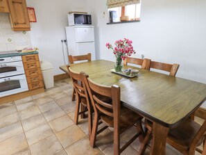Uma cozinha com mesa de jantar, cadeiras, micro-ondas e geladeira.