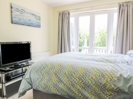 Quarto com cama, televisão sobre suporte, quadro na parede e janela com cortinas.