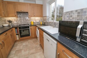 Uma cozinha moderna com armários de madeira, lava-louças, fogão e micro-ondas.