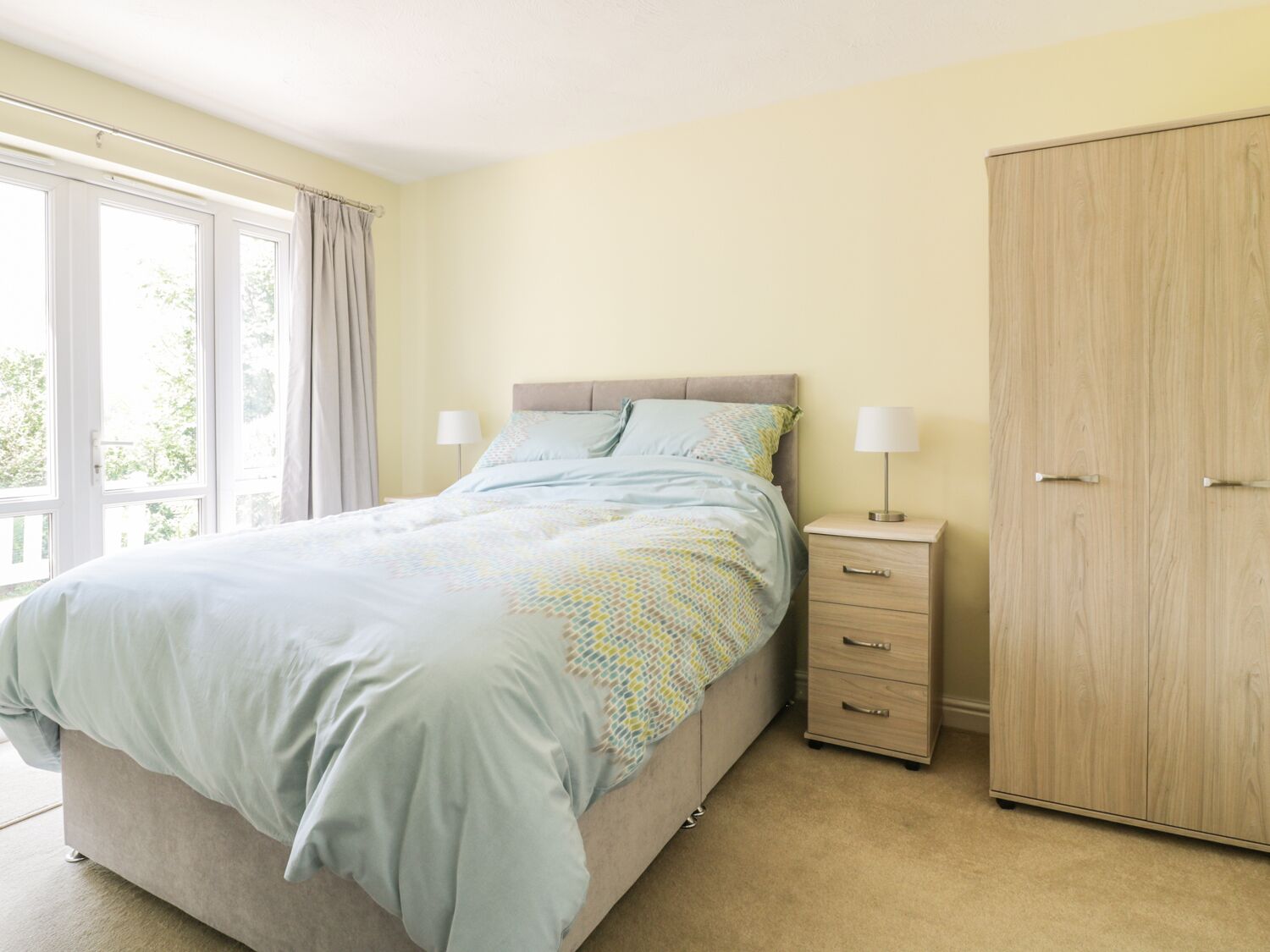 Quarto com cama, abajures, guarda-roupa e janela com cortinas.