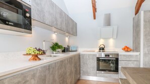 Cozinha moderna com micro-ondas, forno e torradeira embutidos. Balcão de madeira com uma fruteira e uma planta. O chão é de madeira, e a cozinha tem um design minimalista.