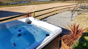 Banheira de hidromassagem com vista para uma praia arenosa e paisagem rural.