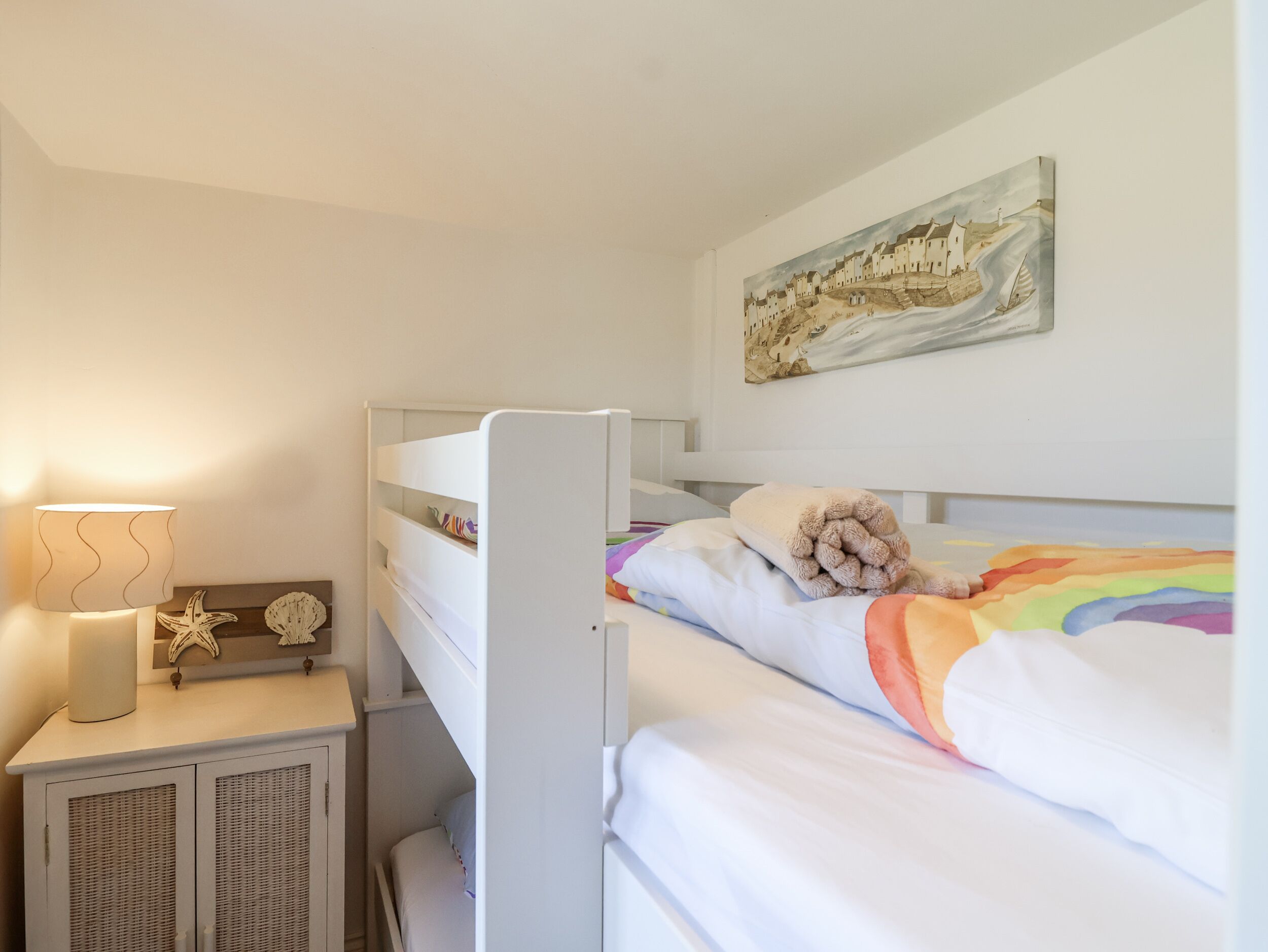 Quarto com beliche, mesa de cabeceira, abajur e um quadro na parede.