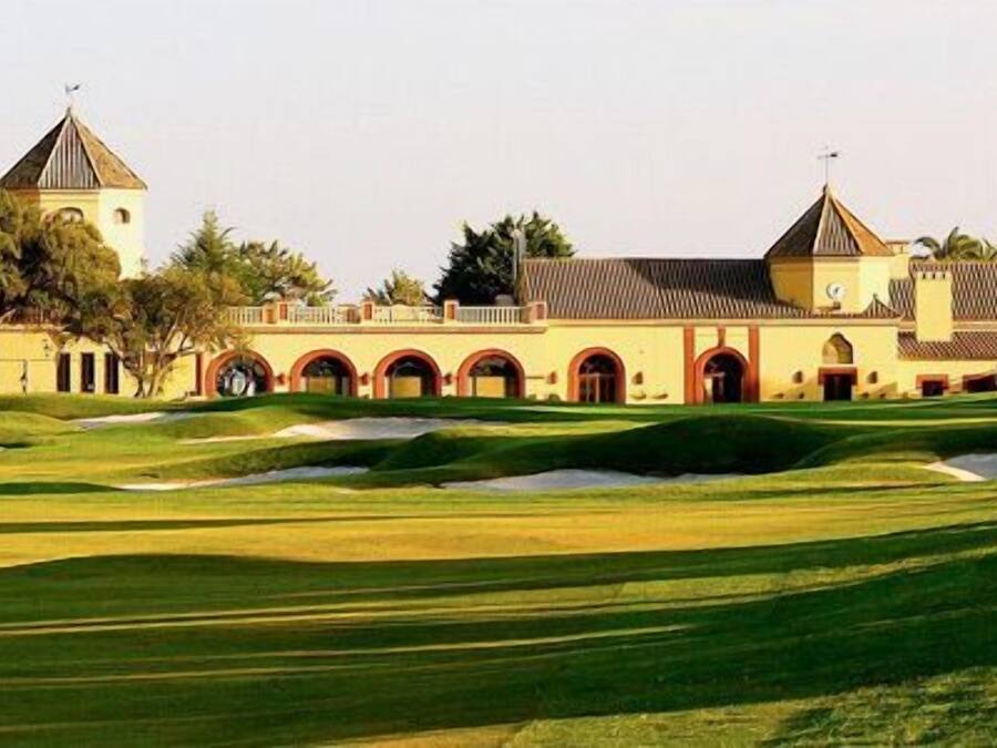 Um campo de golfe com um edifício de janelas em arco e uma torre.