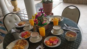 Mesa de vidro com café da manhã, pratos de comida e um vaso de flores.