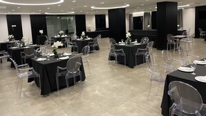 Uma sala de conferências moderna com mesas redondas, cadeiras transparentes e toalhas de mesa pretas.