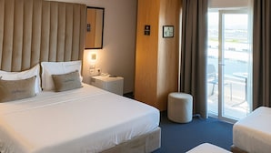 Quarto de hotel com uma cama grande, mesa de cabeceira, mesinha, uma cadeira e vista para o exterior.