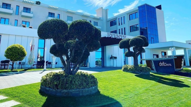 Um hotel com design moderno, apresentando um pátio central com árvores bem aparadas e um gramado bem cuidado.