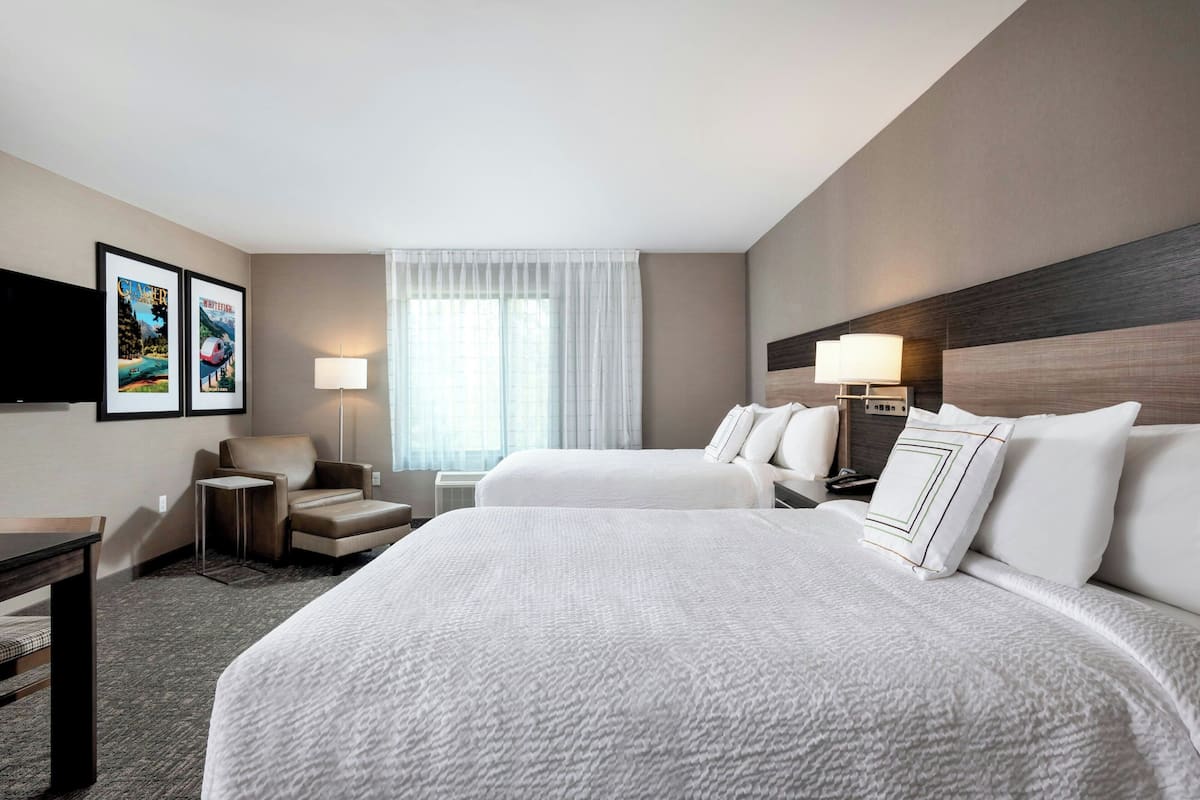 Quarto de hotel com duas camas, uma escrivaninha, uma cadeira, uma televisão e quadros nas paredes.