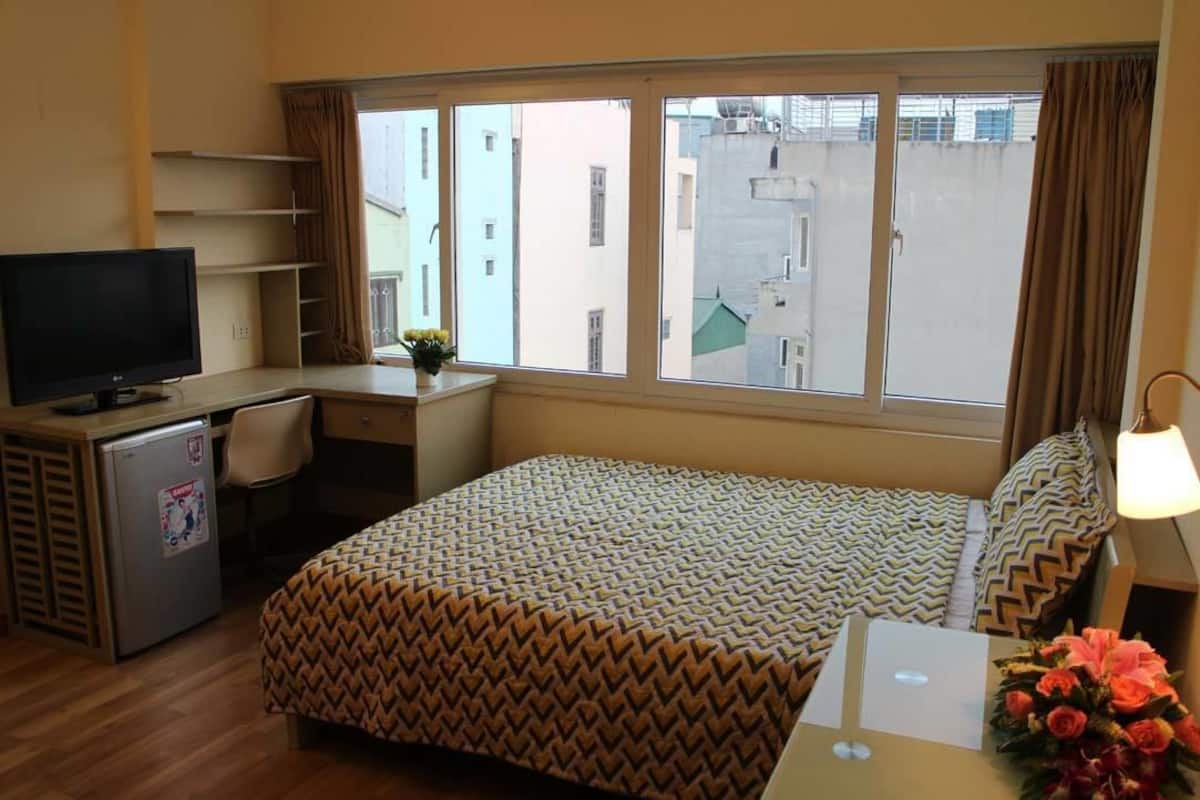 Quarto de hotel com cama, escrivaninha com computador, televisão e janela com cortinas.