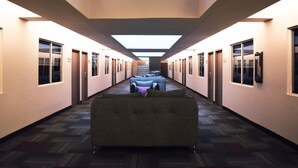 Um corredor de hotel com área de estar central, várias portas e um claraboia.