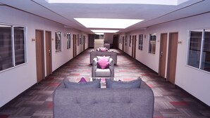 Um corredor de hotel com área de estar central, várias portas e um carpete estampado.