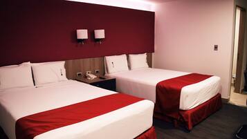 Quarto de hotel com duas camas, cada uma com colcha vermelha e branca, cabeceira de madeira e duas luminárias fixadas na parede.