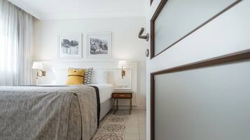 Quarto de hotel com cama, mesas de cabeceira, duas luminárias fixadas na parede e duas quadros emoldurados.