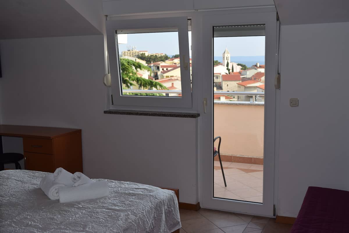 Quarto com cama, escrivaninha e vista para a cidade através de uma porta.