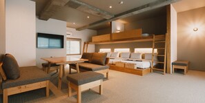 Quarto aconchegante com beliches, TV de tela plana, mesa de madeira e sofá.