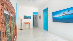 Um corredor com uma porta de madeira, uma porta azul e uma pintura de uma praia tropical.