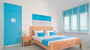 Quarto com cama de madeira, porta azul, mesa de cabeceira com abajur e janela com persianas.