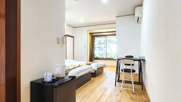 Quarto de hotel compacto com cama, escrivaninha e cadeira. Há uma janela que oferece luz natural e vista para o verde lá fora.