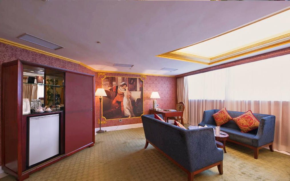 Quarto de hotel com sofá, mesa pequena, armário com espelho e uma grande pintura na parede.