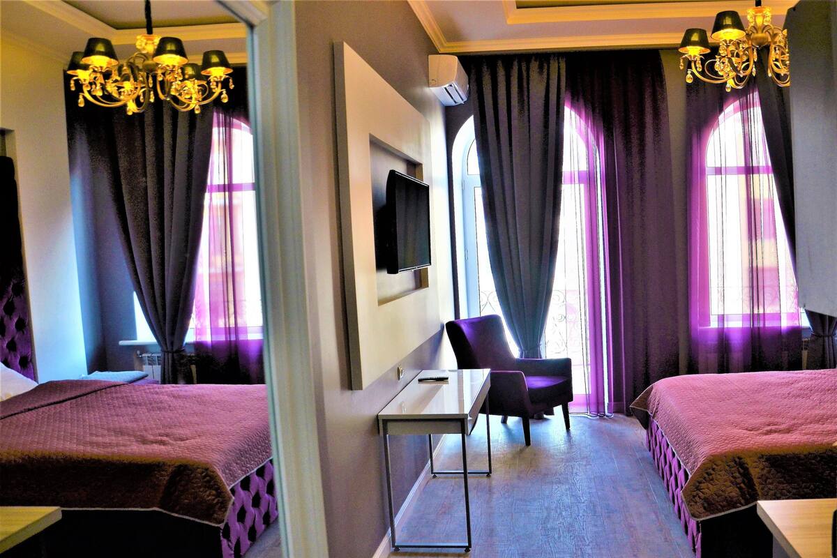 Quarto de hotel com duas camas, uma escrivaninha, uma cadeira e uma televisão na parede.