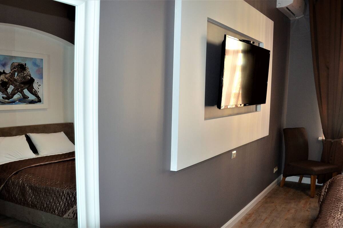 Quarto de hotel com cama, escrivaninha, cadeira, televisão de tela plana na parede e um quadro na parede.