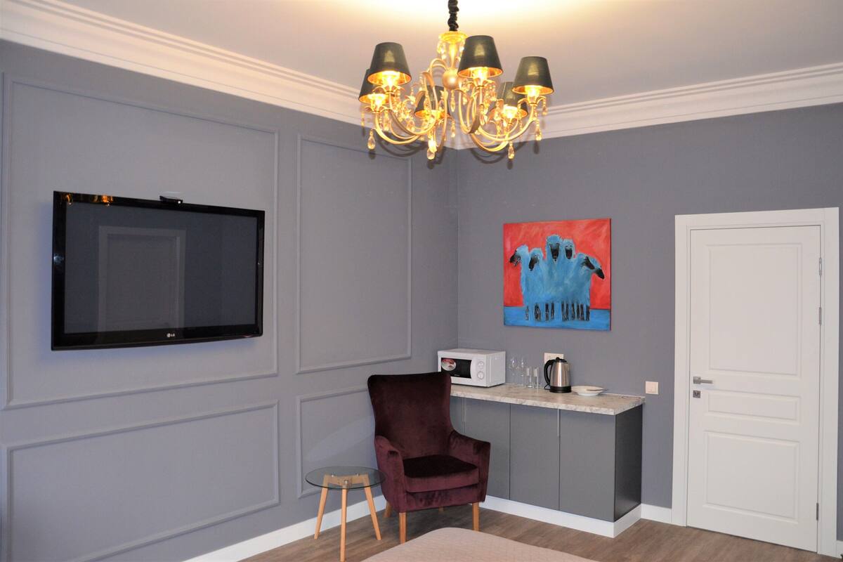 Quarto com televisão de tela plana, uma poltrona de veludo vermelha, micro-ondas, um quadro e uma porta branca.