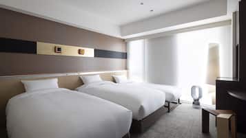 Quarto de hotel com duas camas, uma escrivaninha, uma cadeira e uma janela grande com persianas.