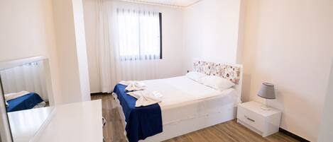 Quarto de hotel com cama, mesa de cabeceira com abajur, espelho e janela com cortinas.