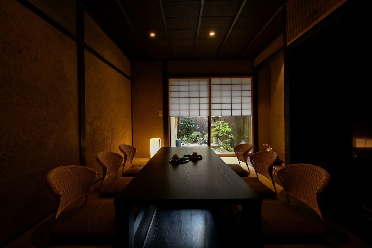 Um quarto japonês tradicional com piso de tatame, uma mesa baixa e quatro tatames dispostos ao redor.