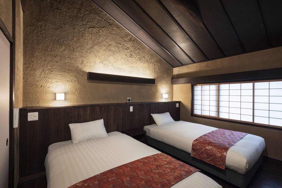 Quarto de hotel com duas camas, cabeceiras de madeira, parede texturizada e janela com vista.