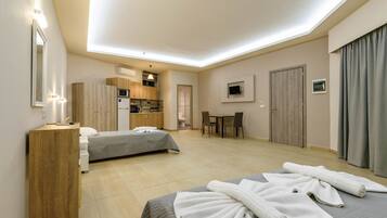 Quarto de hotel com duas camas, uma escrivaninha, uma cozinha compacta e um banheiro.