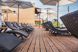 Um deck de madeira com espreguiçadeiras e guarda-sóis, um edifício com fachada bege e um céu claro.