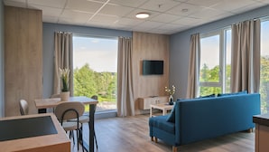 Quarto de hotel moderno com área de refeições, um sofá e uma TV fixada na parede.