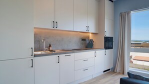 Uma cozinha moderna com armários brancos, bancada cinza e janela com vista.
