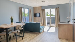 Quarto de hotel moderno com área de refeições, sofá, televisão na parede e varanda com cortinas.