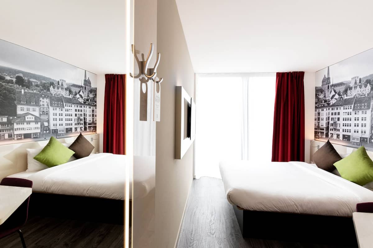 Quarto de hotel com duas camas, vista para o horizonte urbano e design moderno.