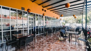 Um espaço de refeições em ambiente interno com mesas, cadeiras, grandes janelas e decorações esféricas penduradas.