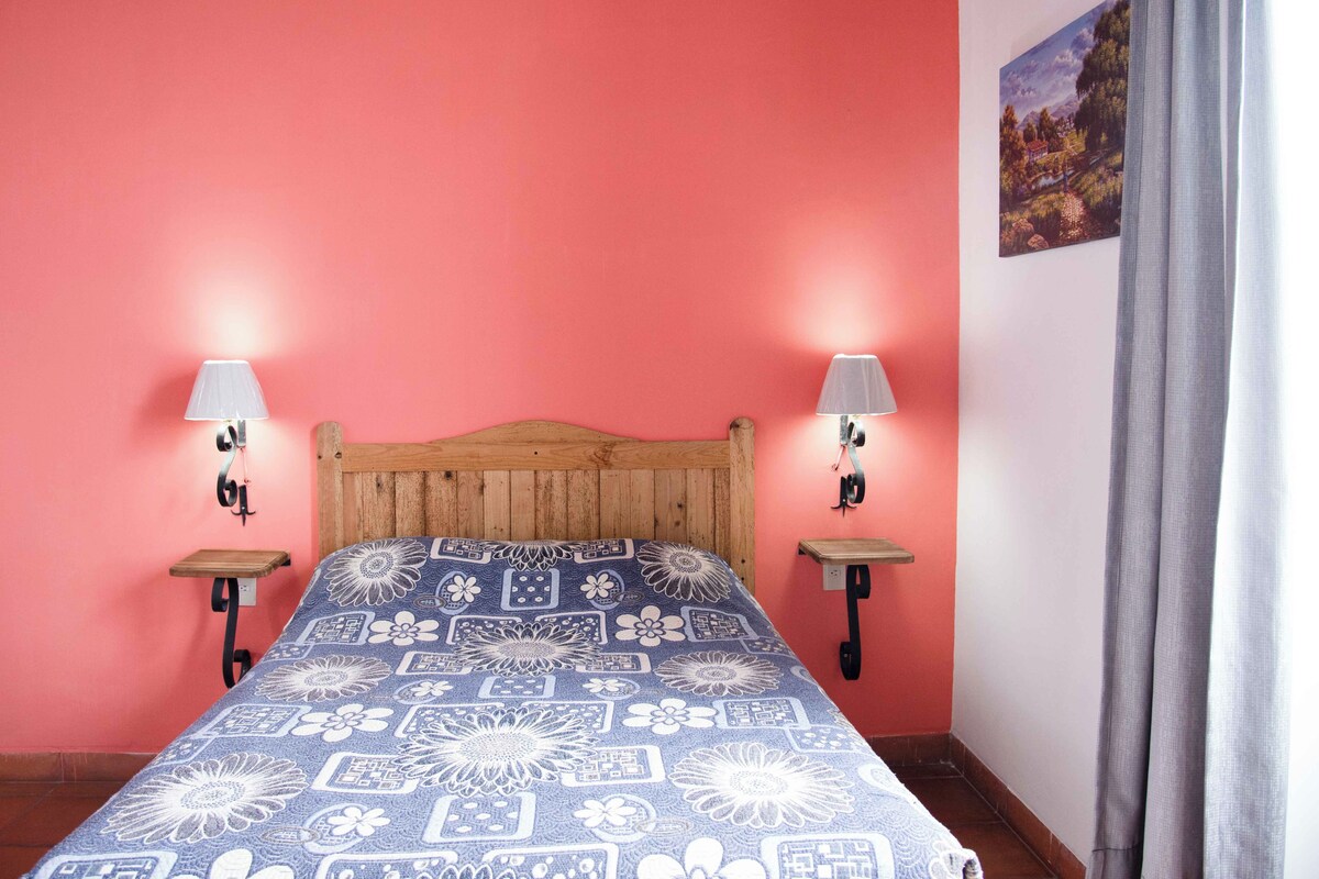 Quarto com cama de cabeceira em madeira, duas luminárias de apoio e um quadro na parede.