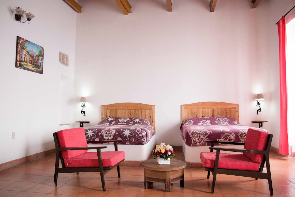 Quarto com duas camas, uma mesinha com um vaso de flores e duas cadeiras.